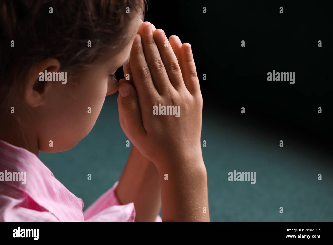 Cute little girl with hands clasped together praying on blurred ...
