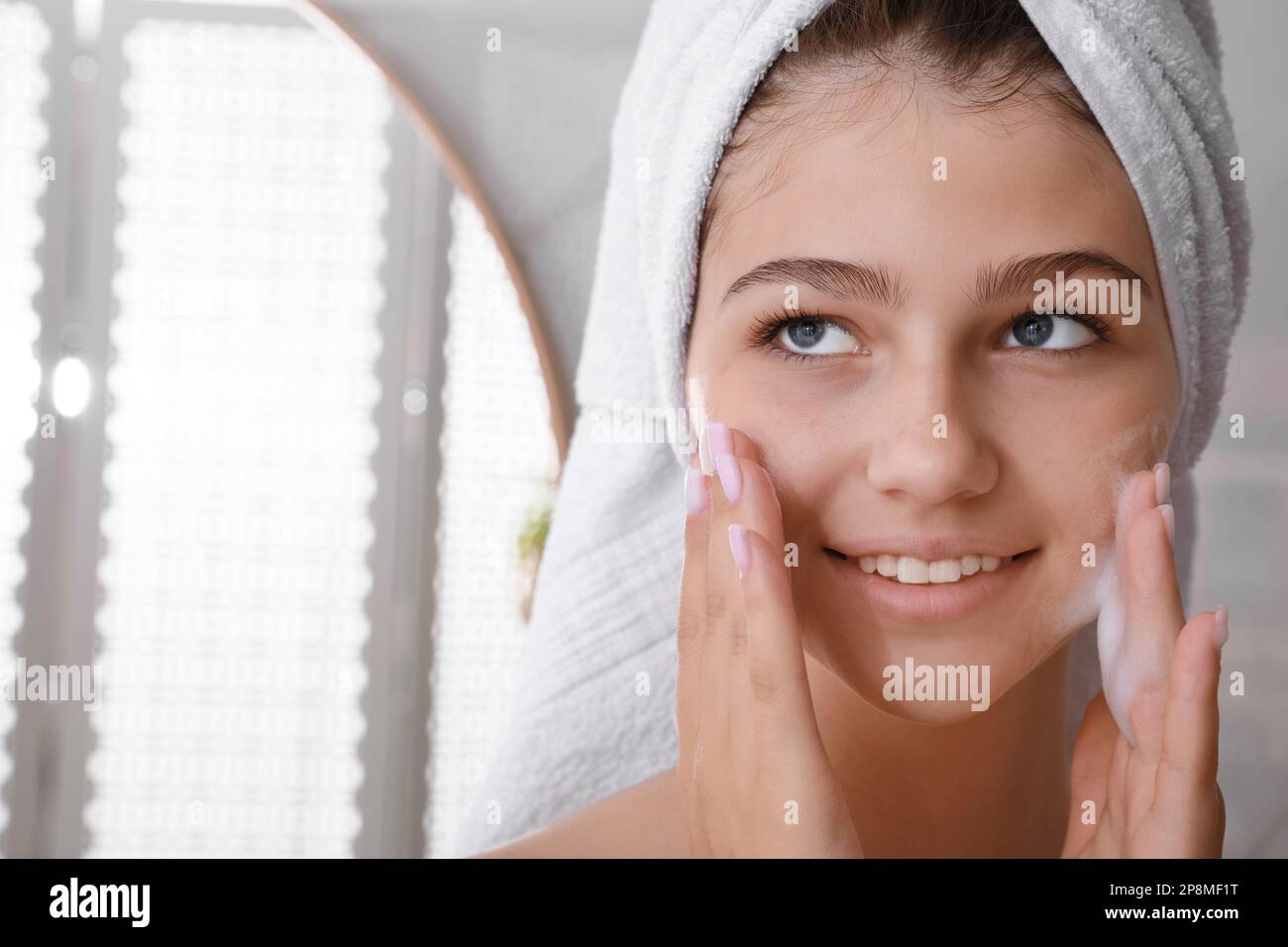 Beautiful teenage girl applying cleansing foam onto face in bathroom ...