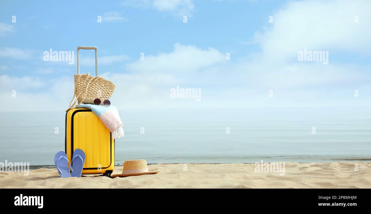 Yellow suitcase with beach items on sandy seashore, space for text ...