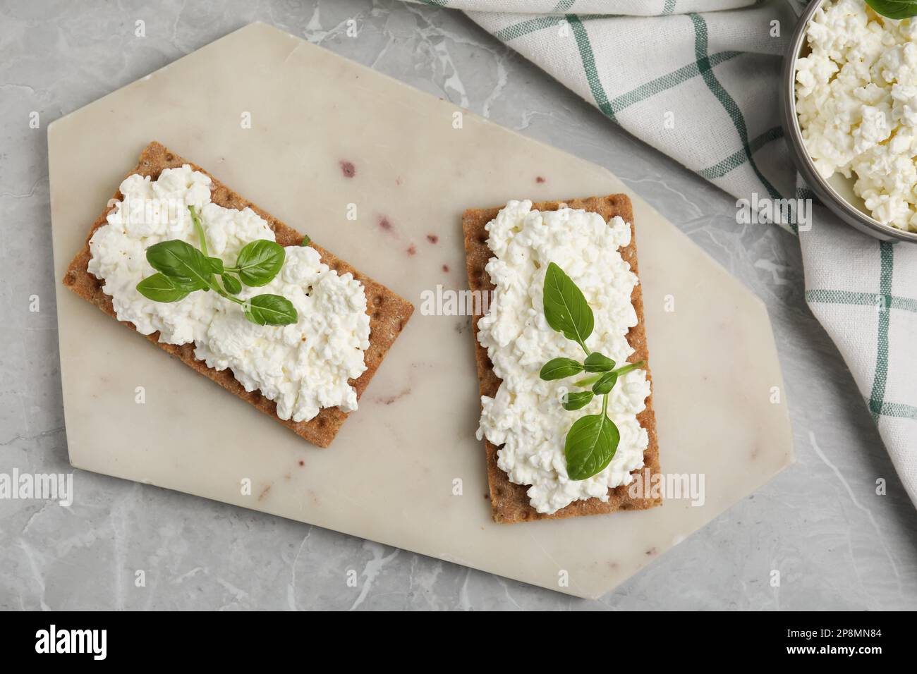 Crispy crackers with cottage cheese and basil on light grey marble ...