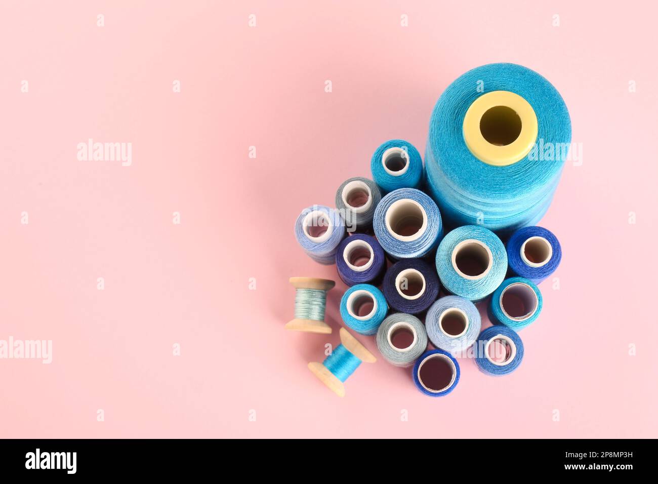 Different shades of blue sewing threads on pink background, flat lay ...