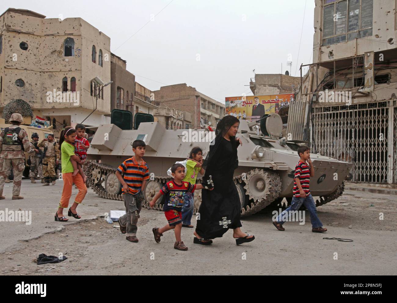 An Iraqi woman walks with children as Iraqi soldiers are seen at the ...