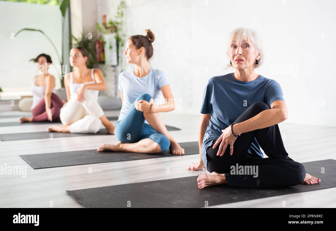 Relaxed positive old woman sitting in twisted position during group ...