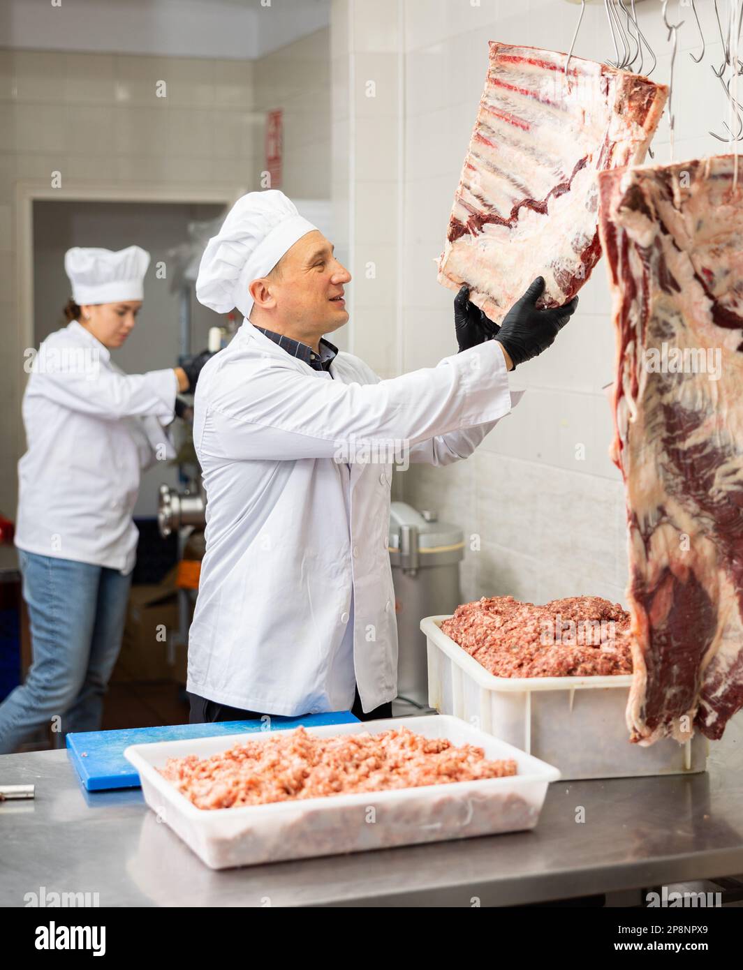 Positive male butcher preparing big piece of beef meat in butcher shop ...