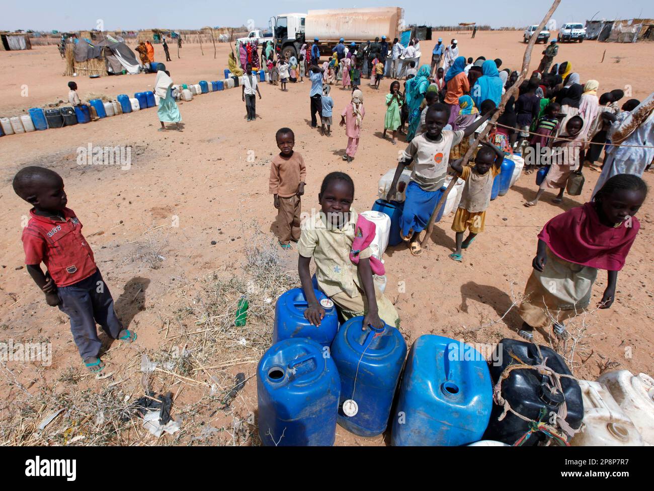 Sudanese refugees line up for water while a UNAMID truck carrying water ...