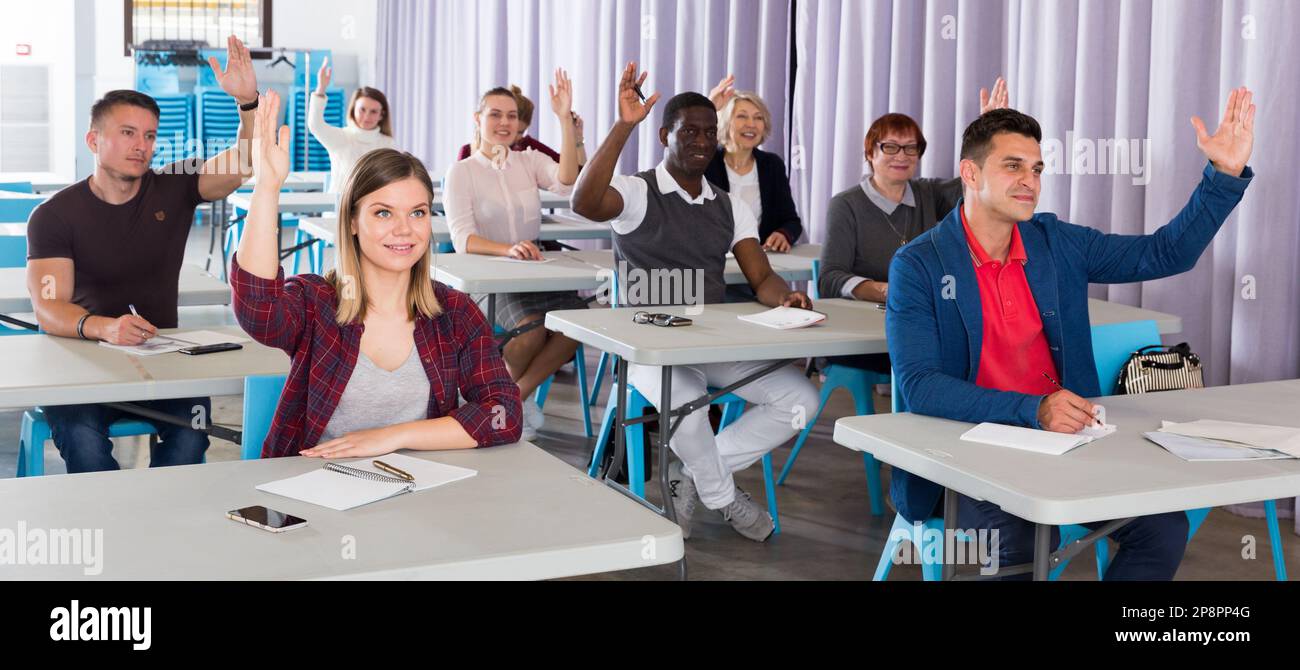 Adult people raising hands in classroom Stock Photo - Alamy
