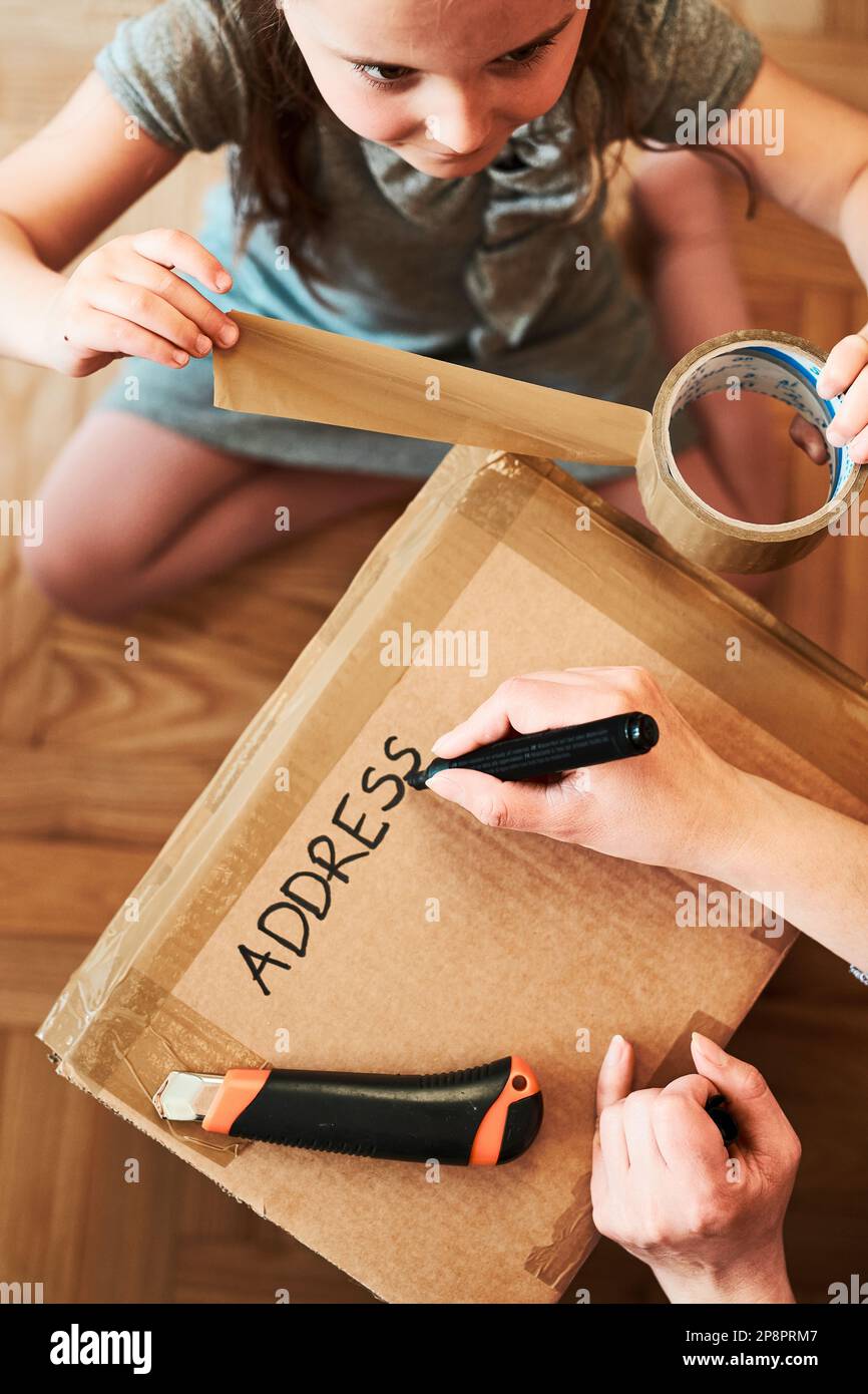 Woman writing an address on a cardboard box parcel in room at home ...