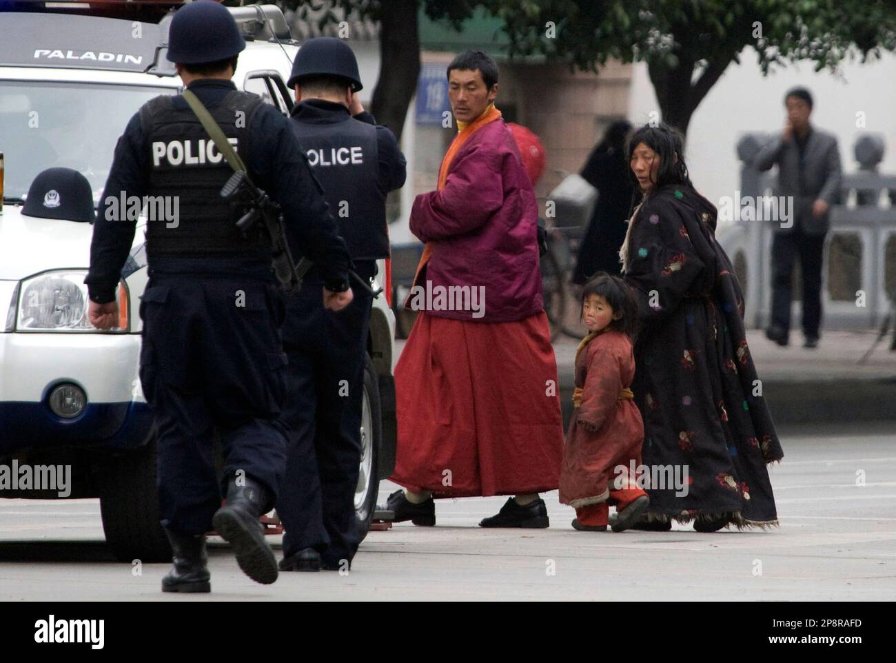 Tibetans walk past heavily armed police officers manning a checkpoint ...