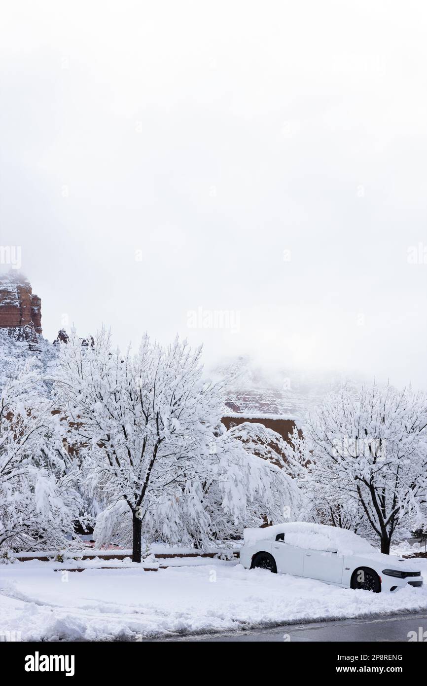 A white car in deep snow in a parking lot, with red rock mountains in ...