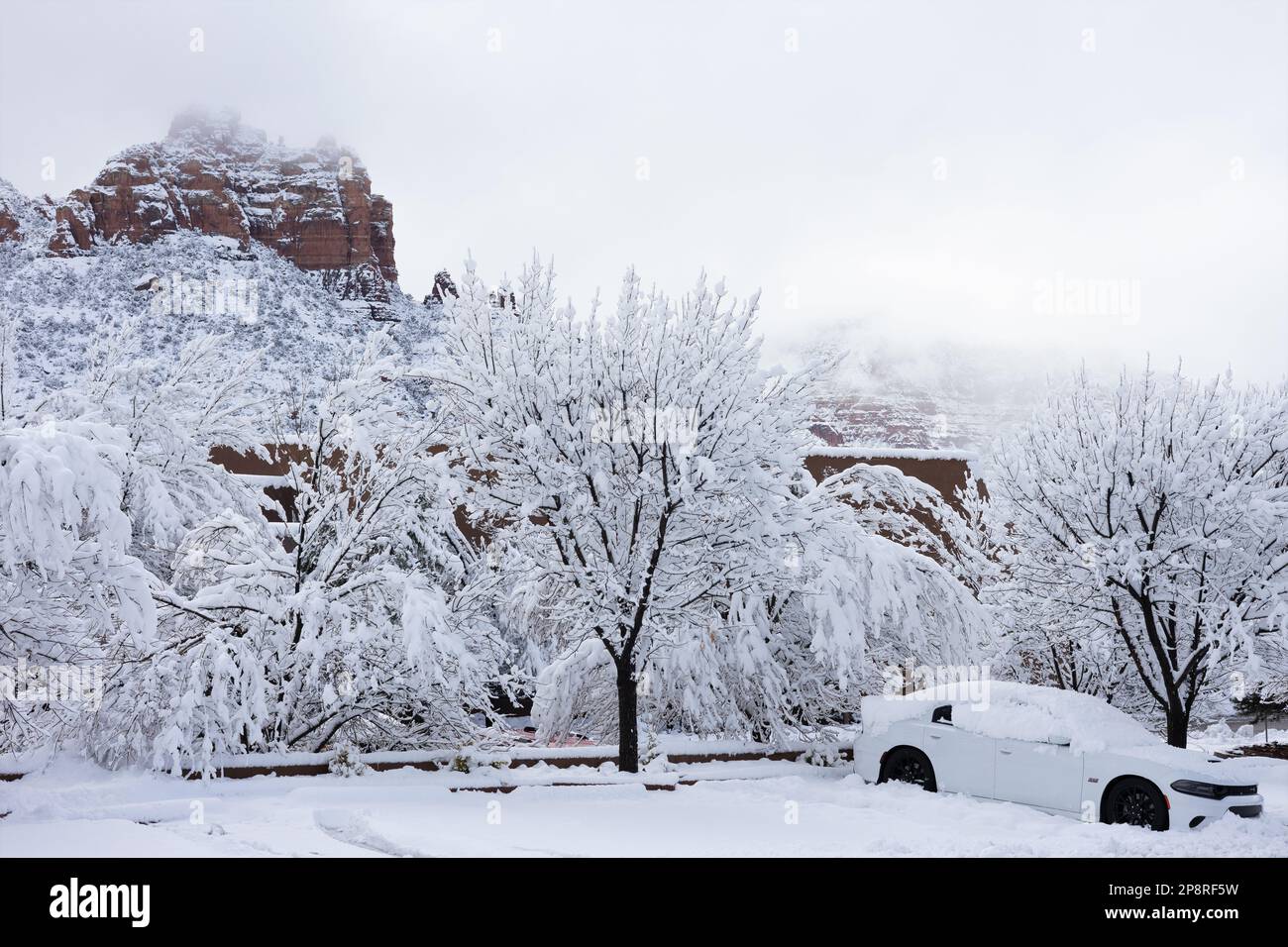A white car in deep snow in a parking lot, with red rock mountains in ...