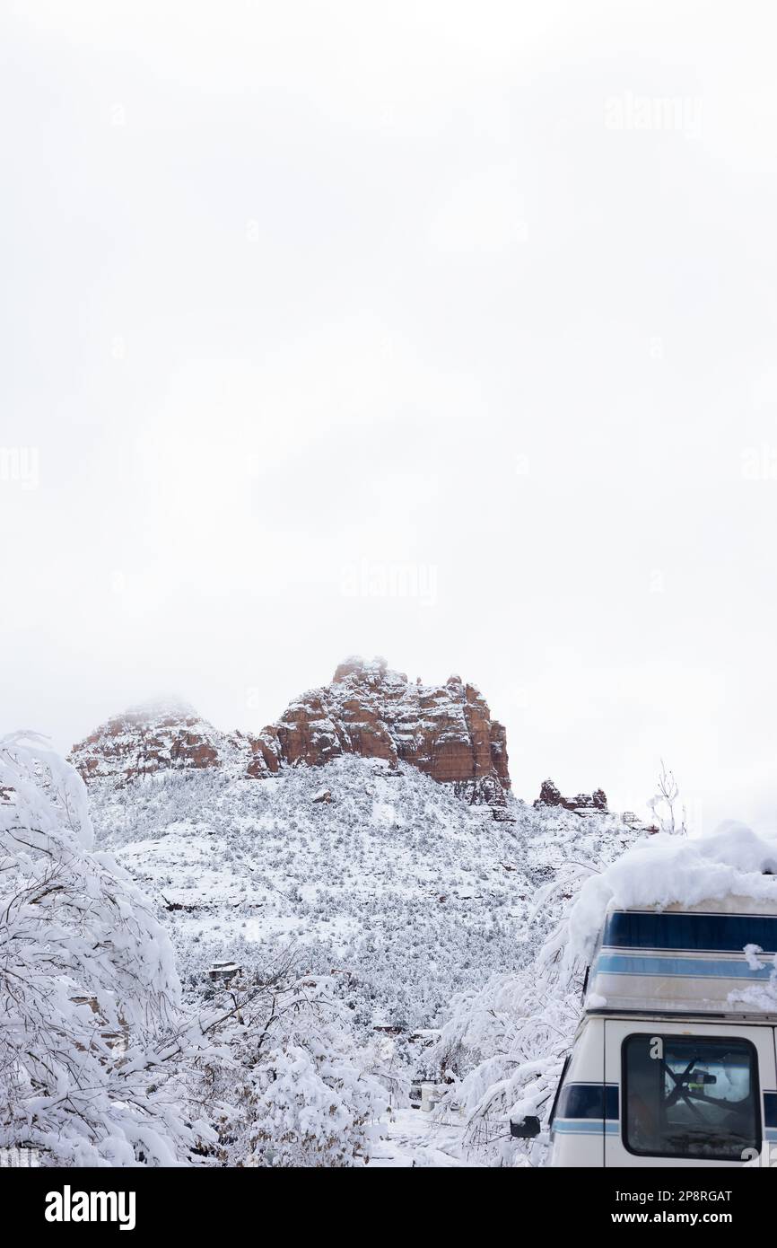 A camper van covered in deep snow, with snowy red rock mountains in the ...