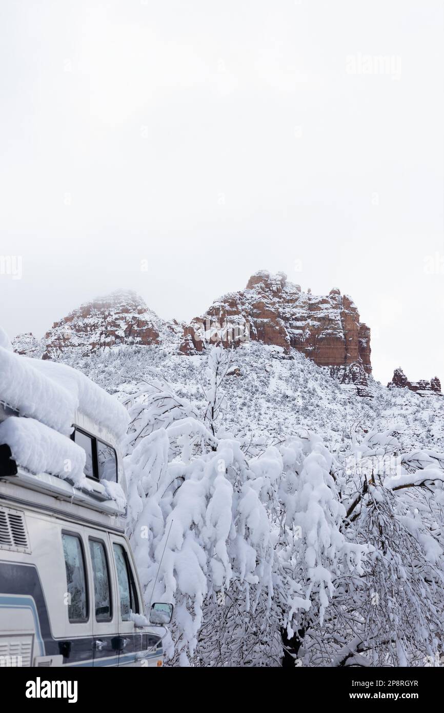 A camper van covered in deep snow, with snowy red rock mountains in the ...
