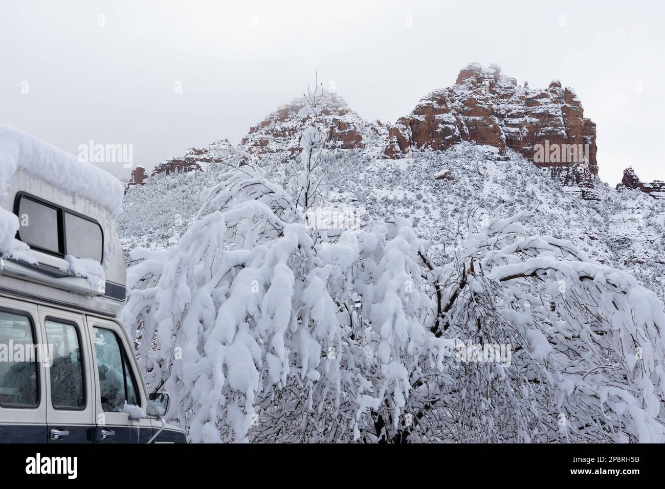 A camper van covered in deep snow, with snowy red rock mountains in the ...