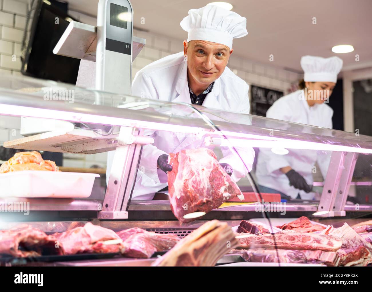 Happy male butcher holding big chunk of beef meat in meat section of ...