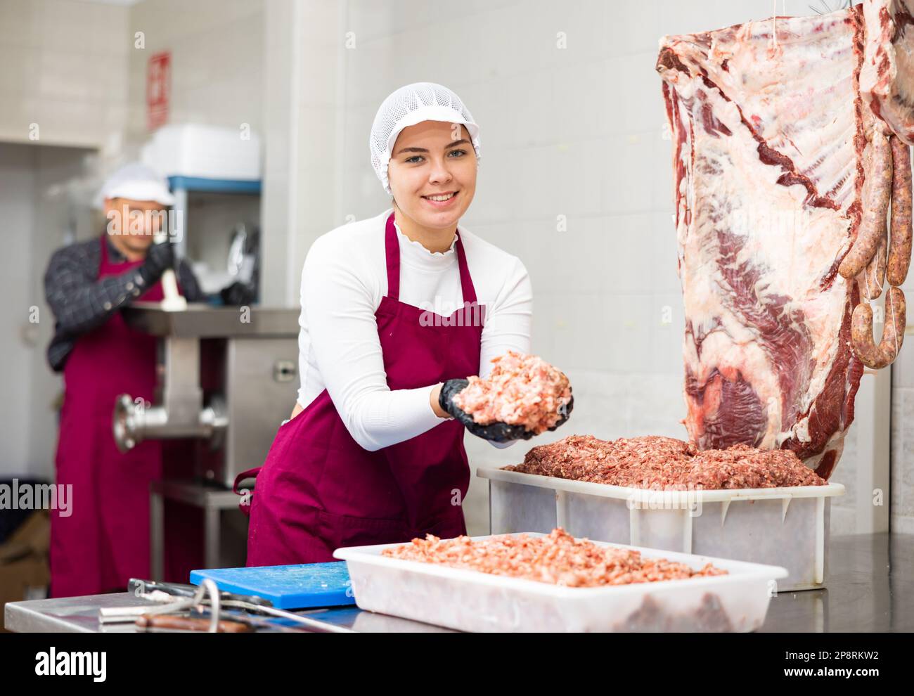 Young female butcher showing how minced meat is prepared in butchery ...