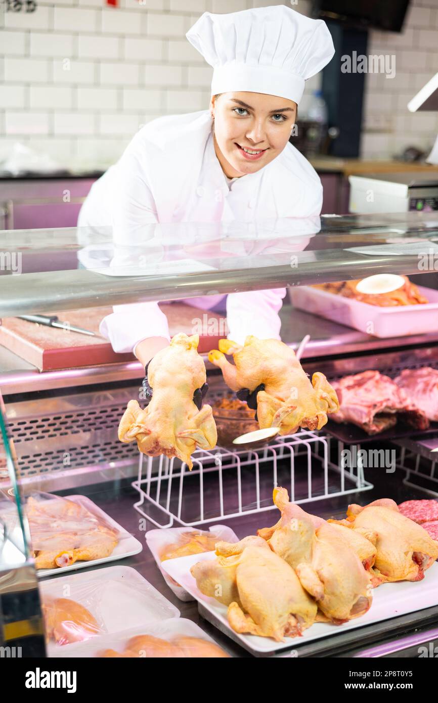 Smiling female butcher offering to sell whole chicken in butcher shop ...