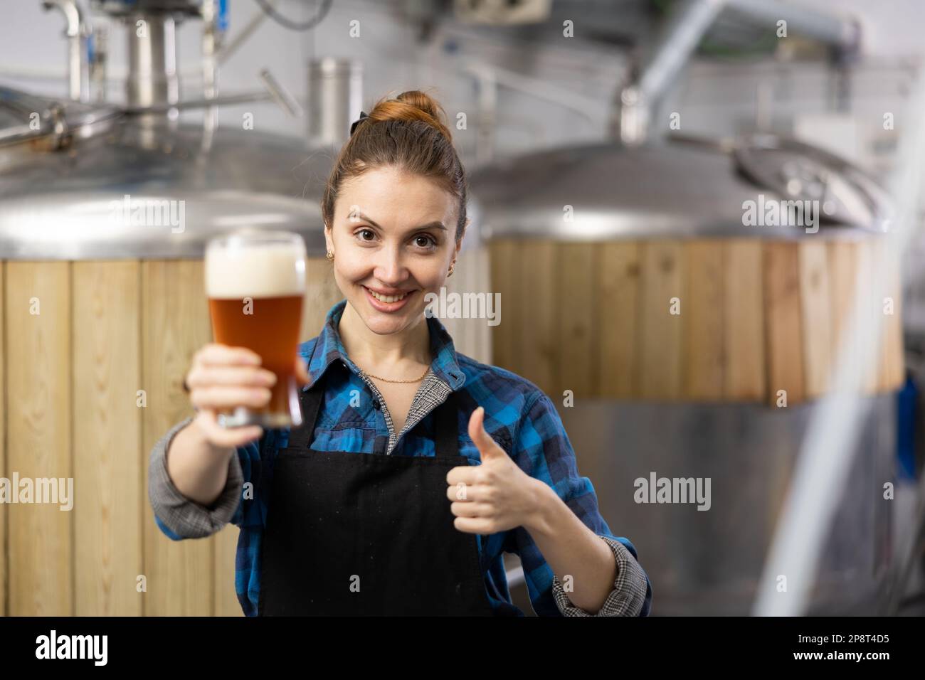 Female brewer is standing with beer with foam in glass on workplace ...