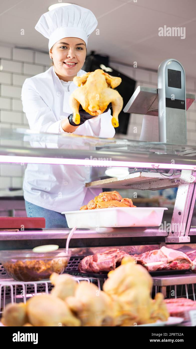 Female butcher laying broiler chickens in display case Stock Photo - Alamy