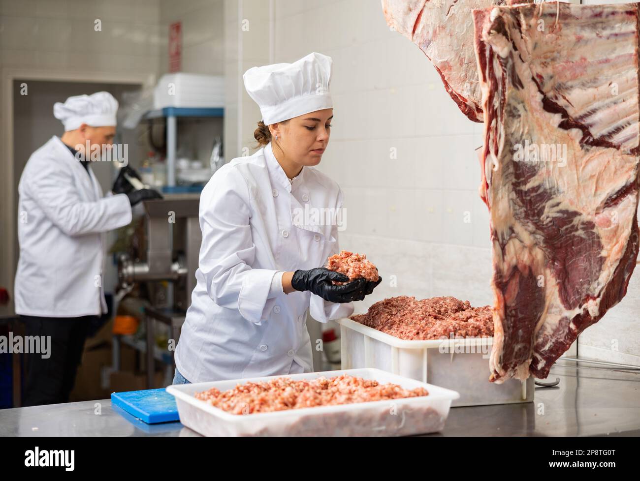 Happy female butcher holding minced beef in meat section of supermarket ...