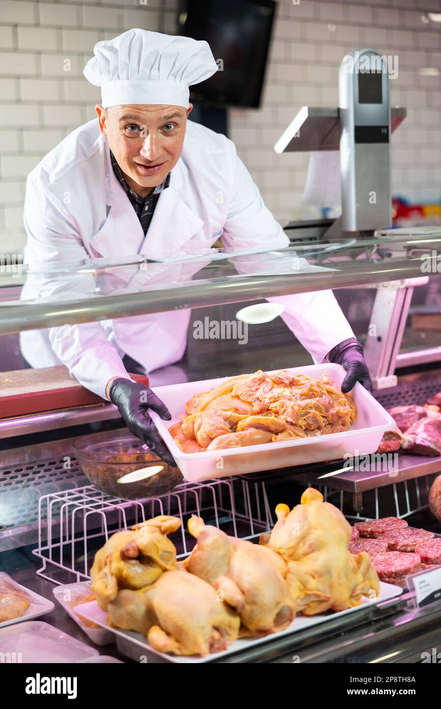 Butcher placing tray with raw chicken fillet on display Stock Photo - Alamy