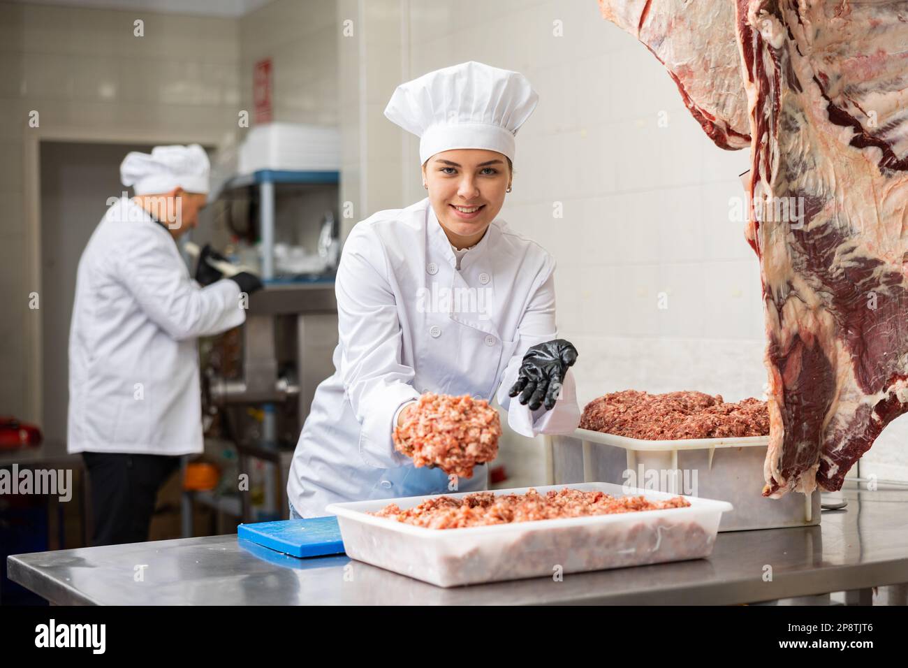 Young female butcher showing how minced meat is prepared in butchery ...