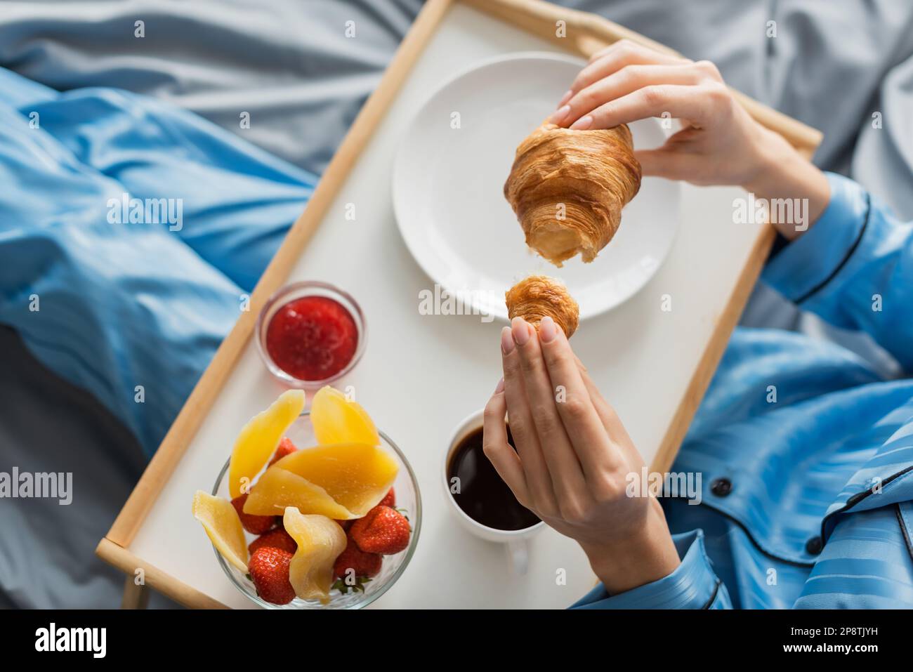 top view of cropped woman holding fresh croissant near tray while ...