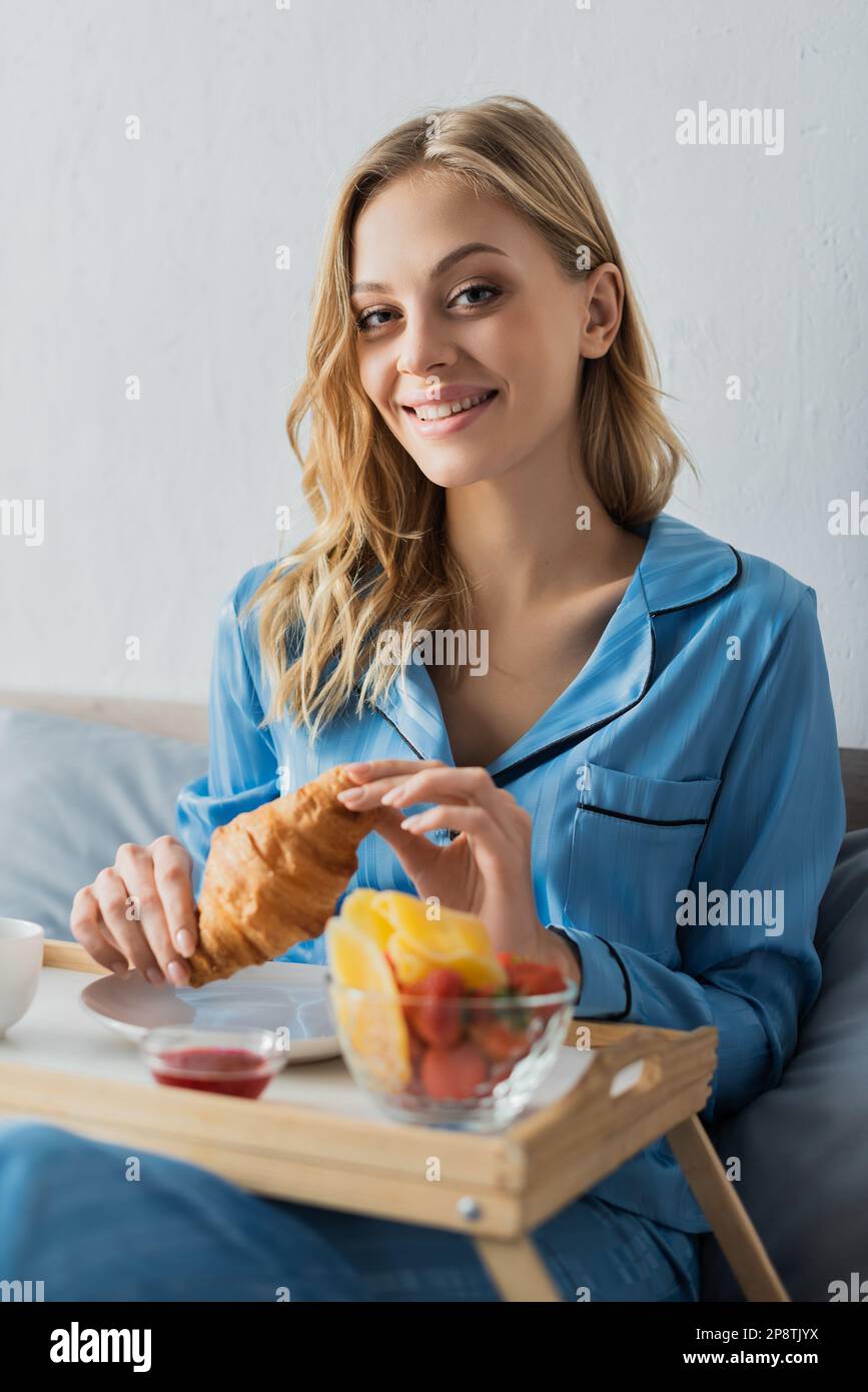 pretty woman in blue pajama holding fresh croissant near tray while ...
