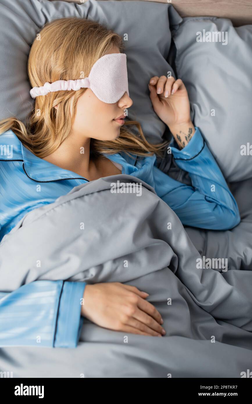 overhead view of blonde woman in sleeping mask and silk pajama resting ...