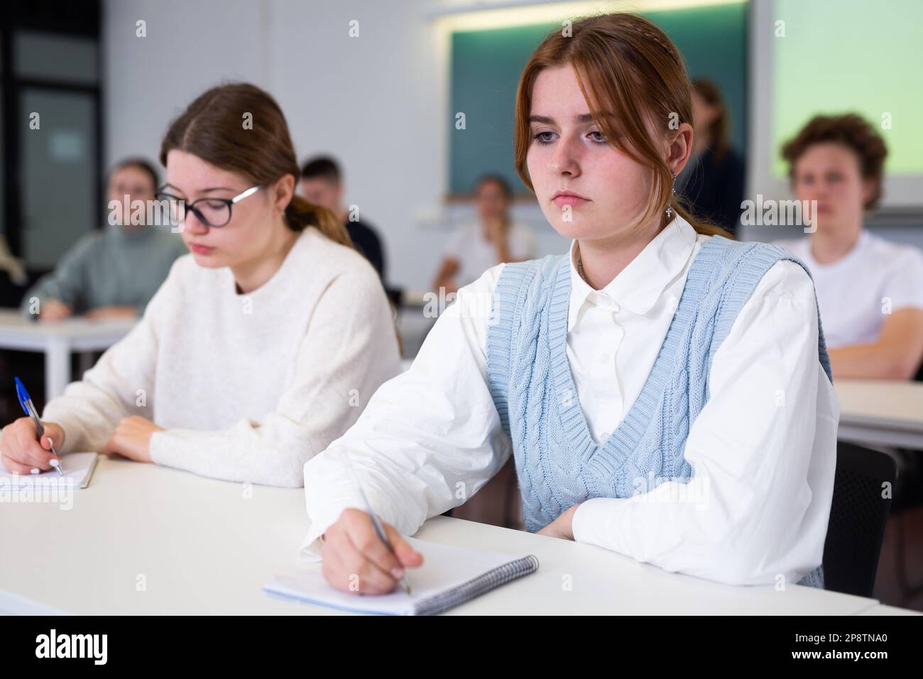 College students sit at desk and write in textbook Stock Photo - Alamy