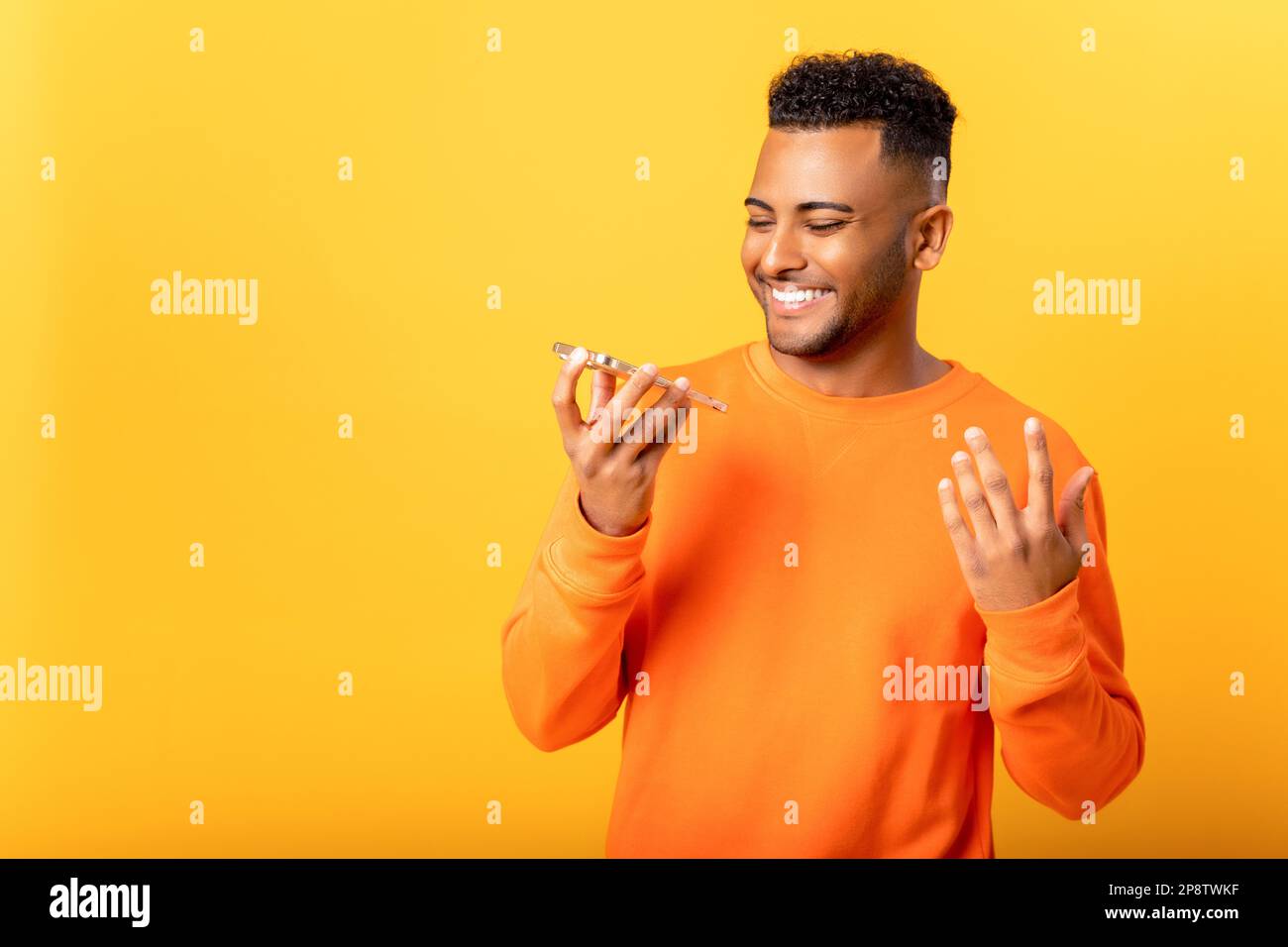 Smiling Indian man is holding smartphone and talking in mic, recording ...