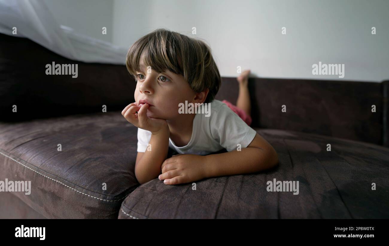 Child laid on couch at home watching media on TV. Portrait of one ...