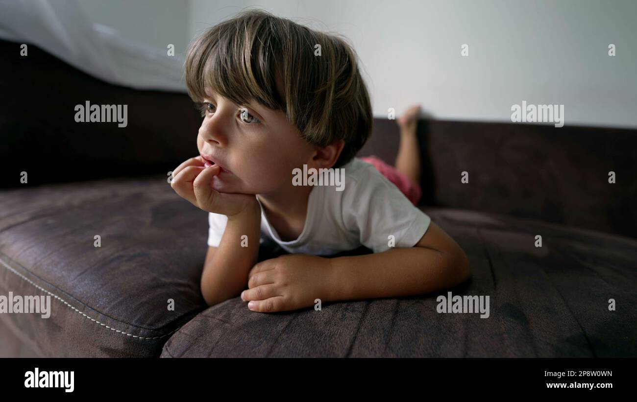 Child laid on couch at home watching media on TV. Portrait of one ...
