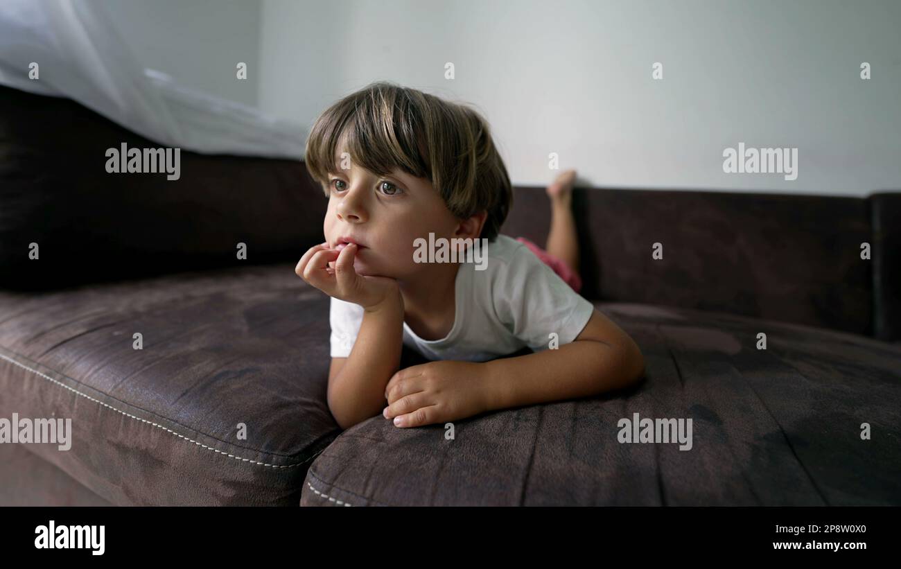 Child laid on couch at home watching media on TV. Portrait of one ...
