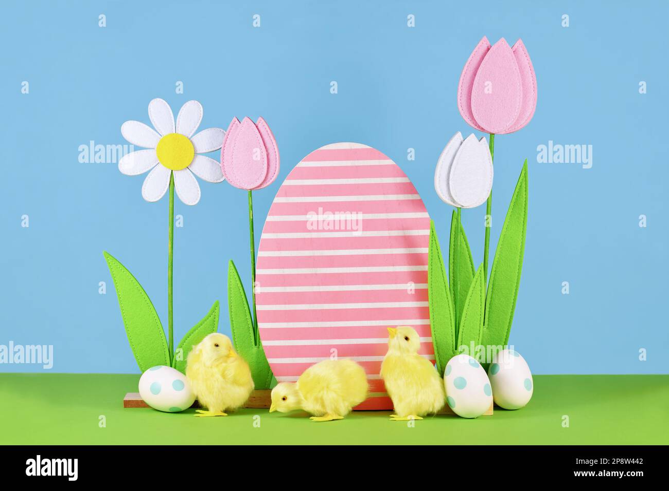Felt spring flowers and wooden Easter egg with chicks in front of blue ...