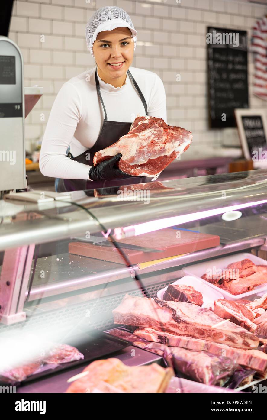 Happy female butcher holding big chunk of beef meat in meat section of ...
