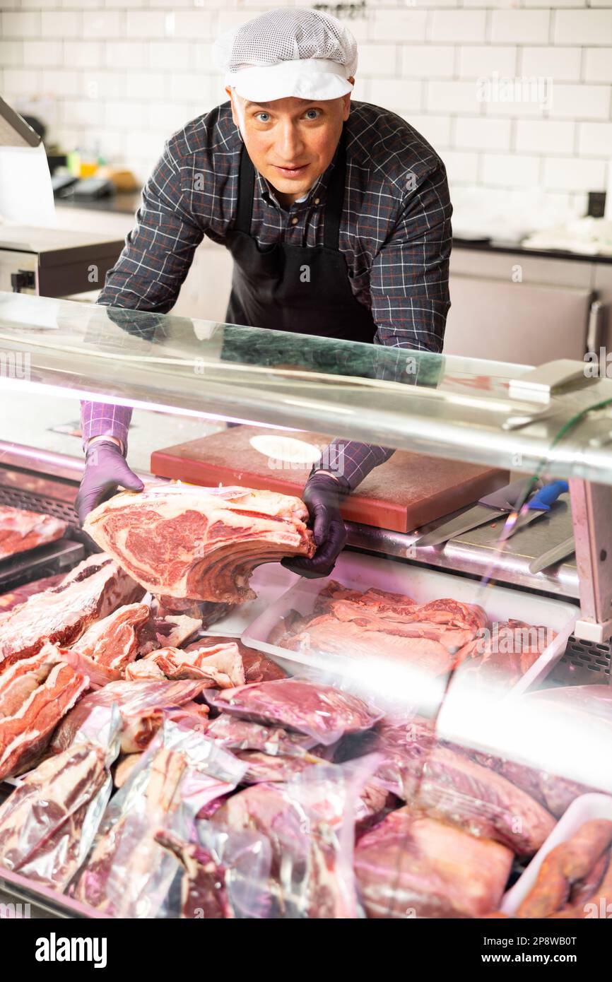 Adult man puts beef ribs in showcase Stock Photo - Alamy