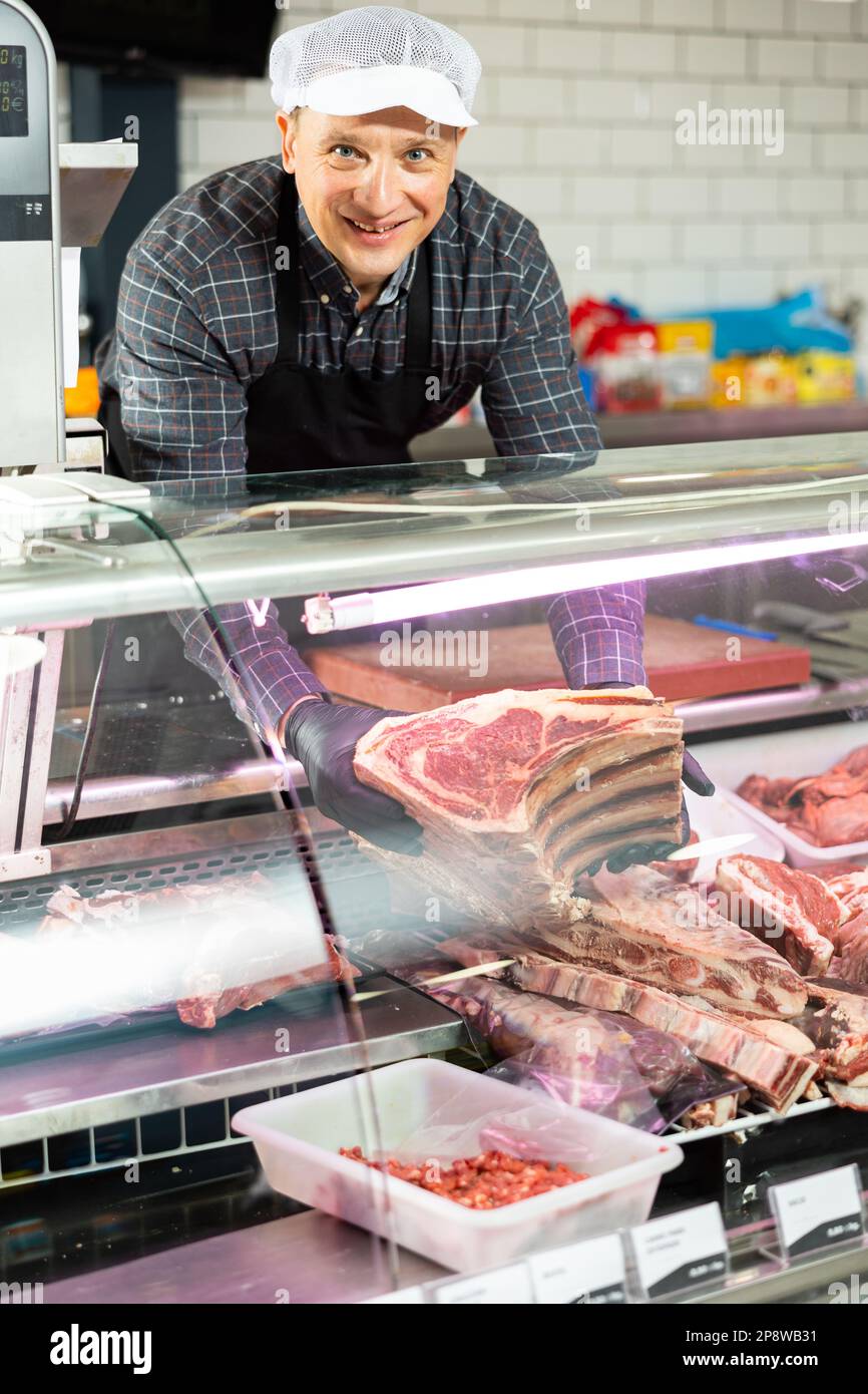 Adult man puts beef ribs in showcase Stock Photo - Alamy