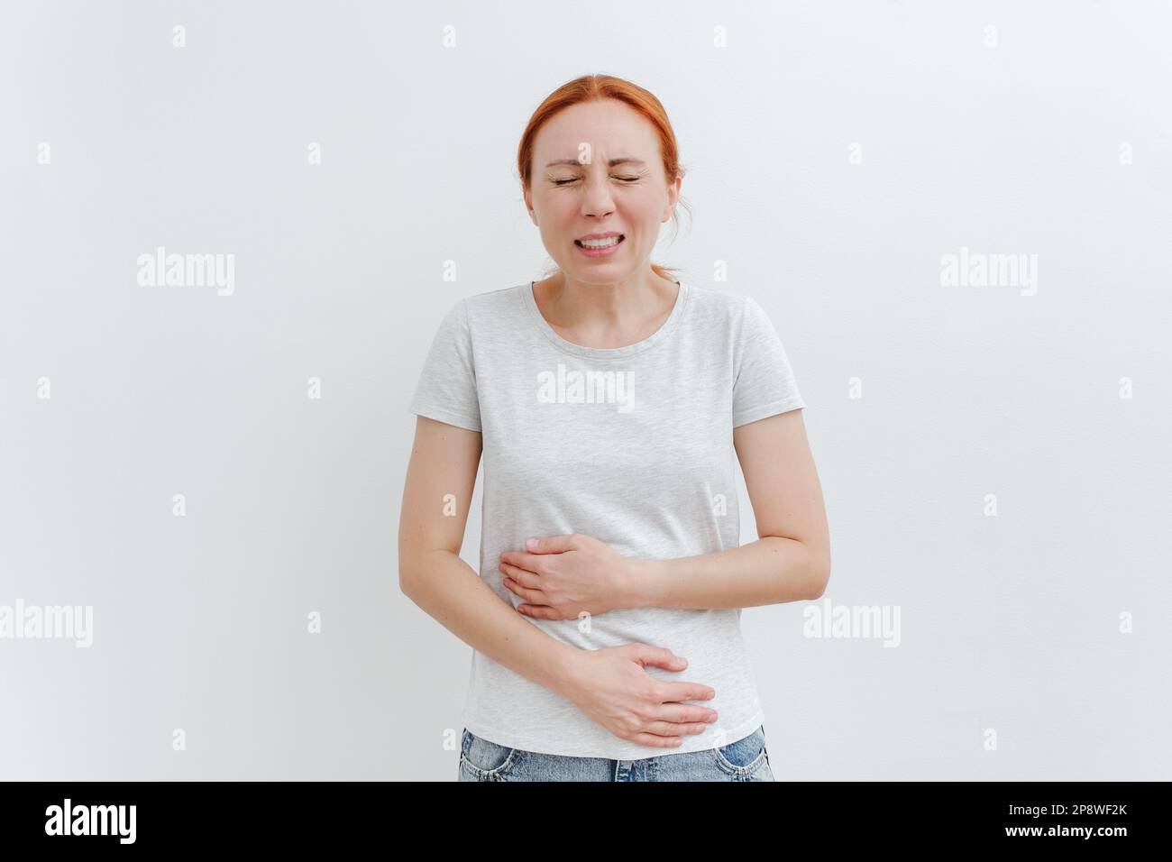 A young woman holds on to her stomach in pain. Digestive problems ...