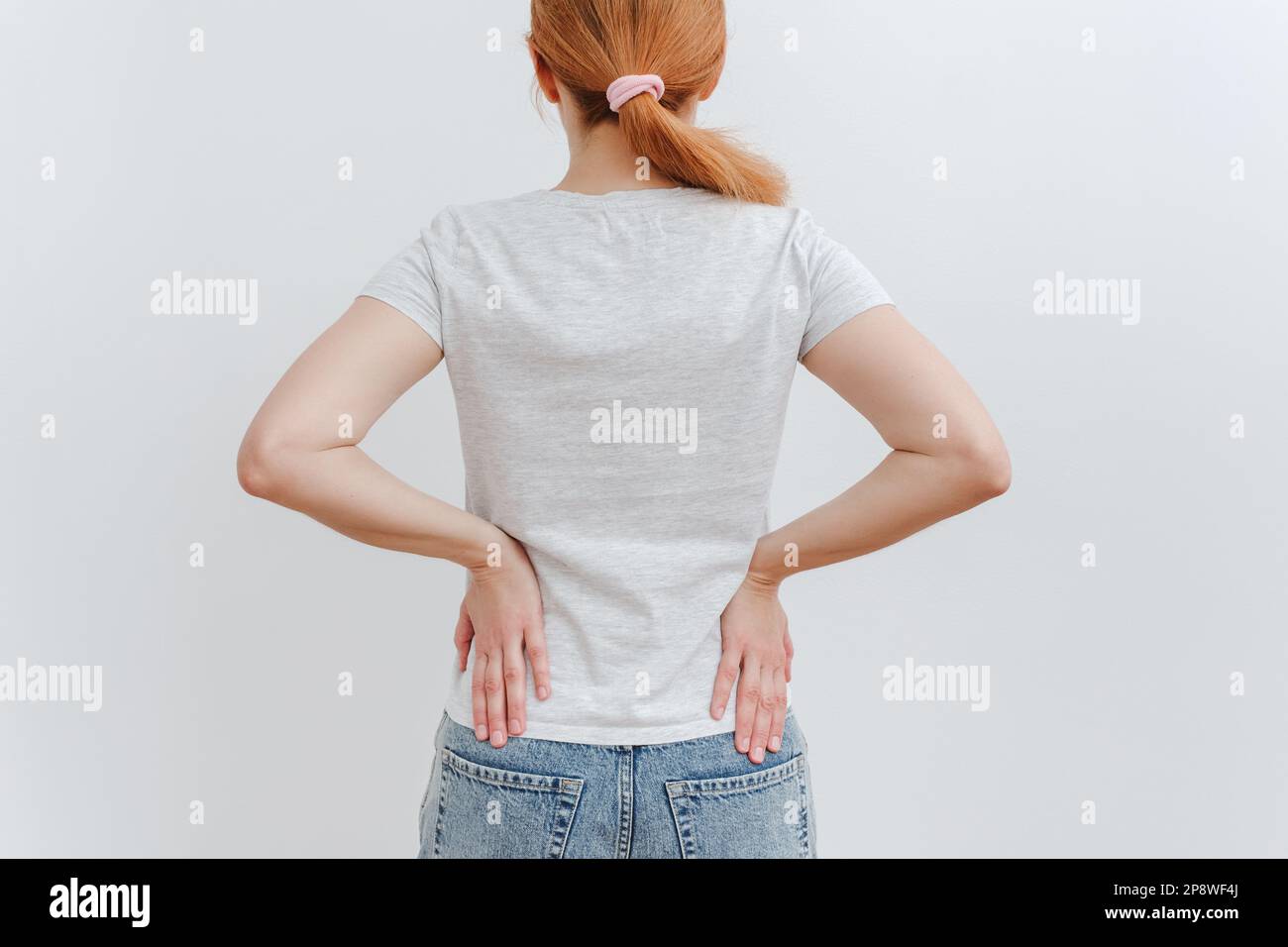 A young woman holding on to her back in pain against a white background ...