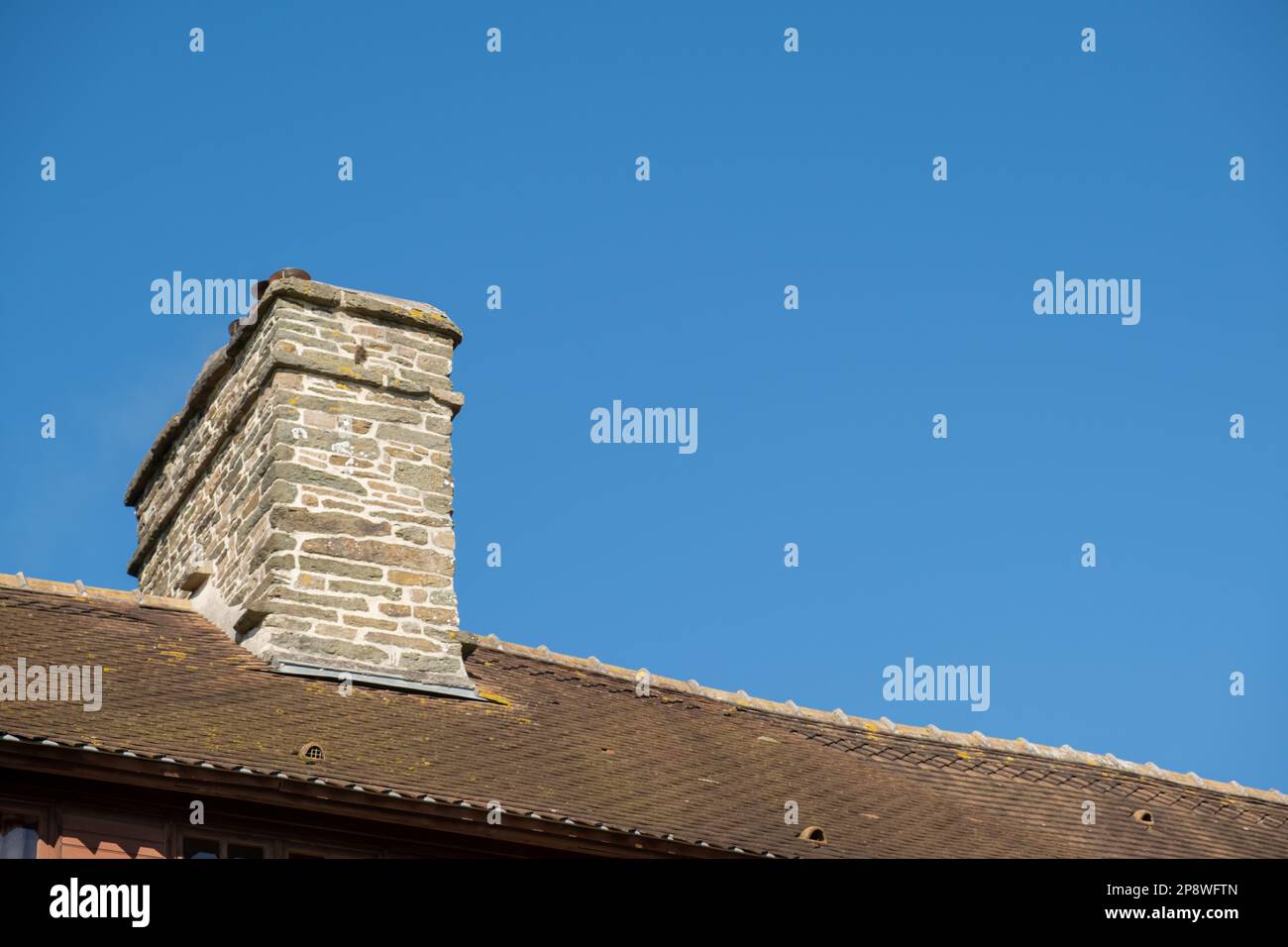 Stone chimney and part of roof made of tiles of old house against blue ...