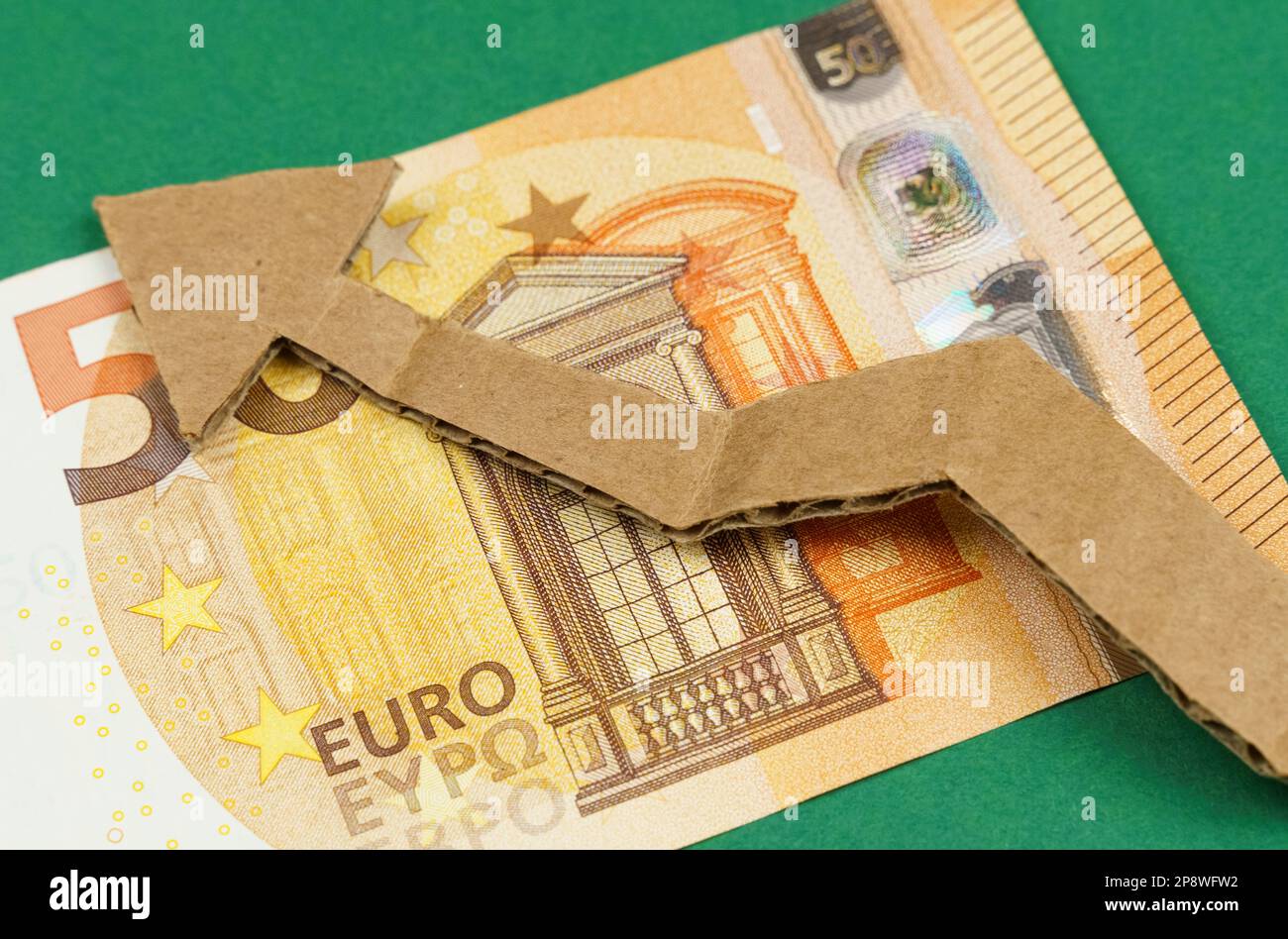 Euro banknotes and a cardboard arrow pointing up lie on a green surface ...