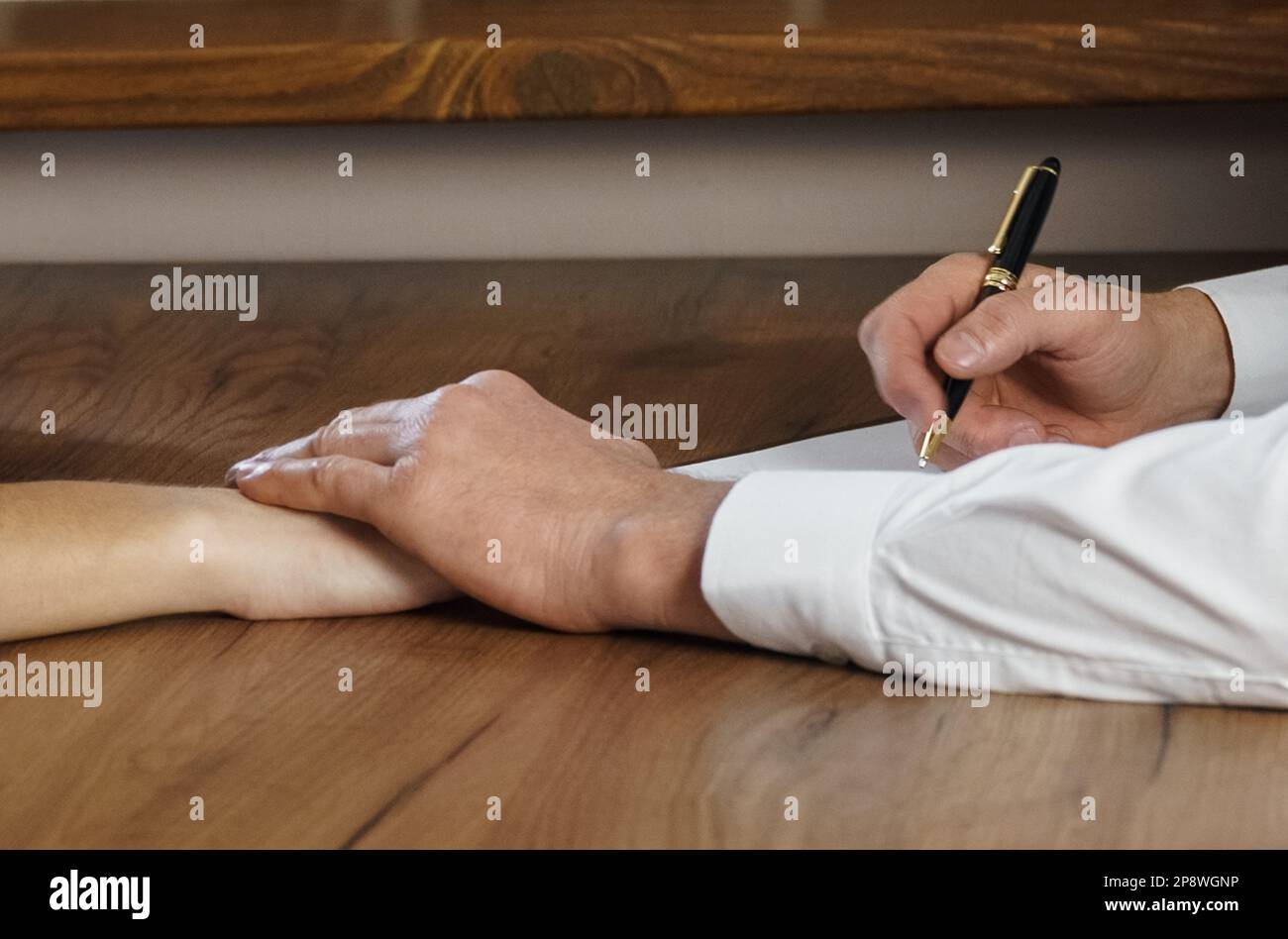 Close-up of a compassionate male doctor holding the hands of a tense ...