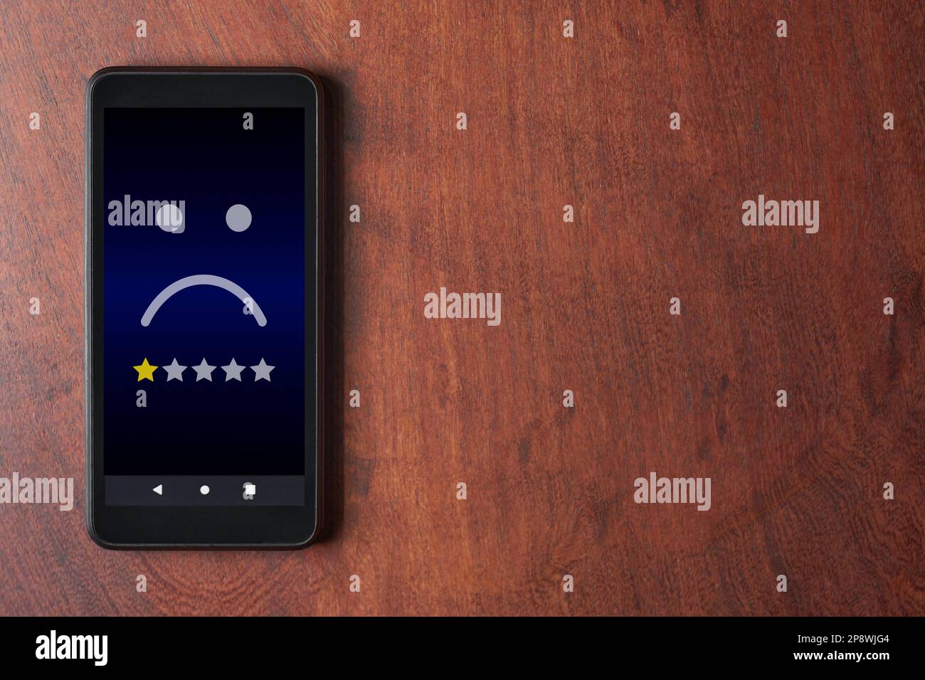 Mobile phone with sad face and one star rating on wooden table with ...