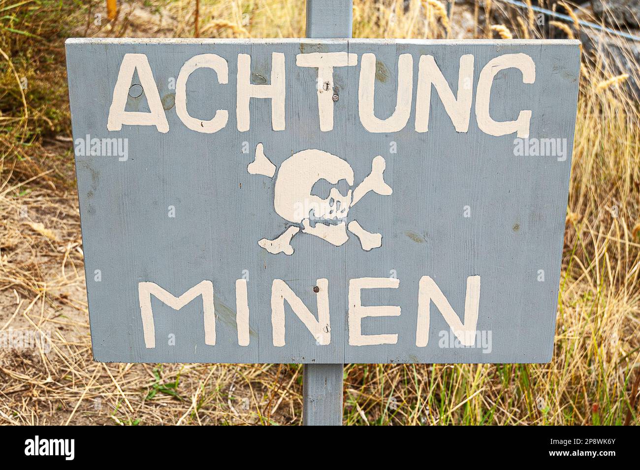 light gray wooden sign with in German language a warning for mines ...