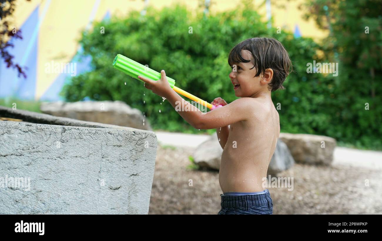 Spraying water at kid during foam toy gun water fight outside in summer ...