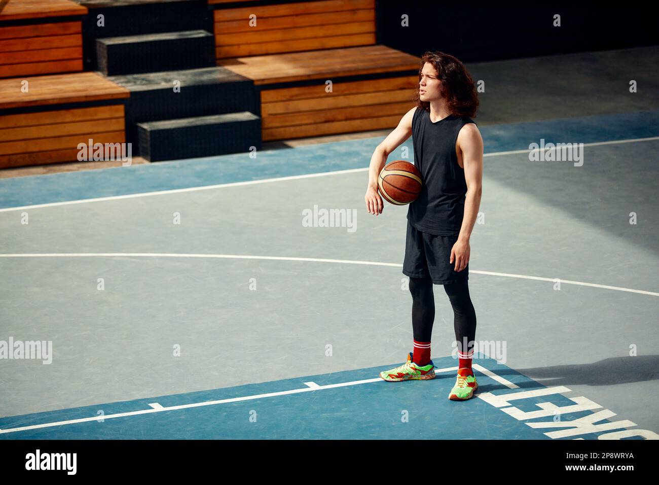 Sports guy on the basketball court, a guy with long hair trains with ...