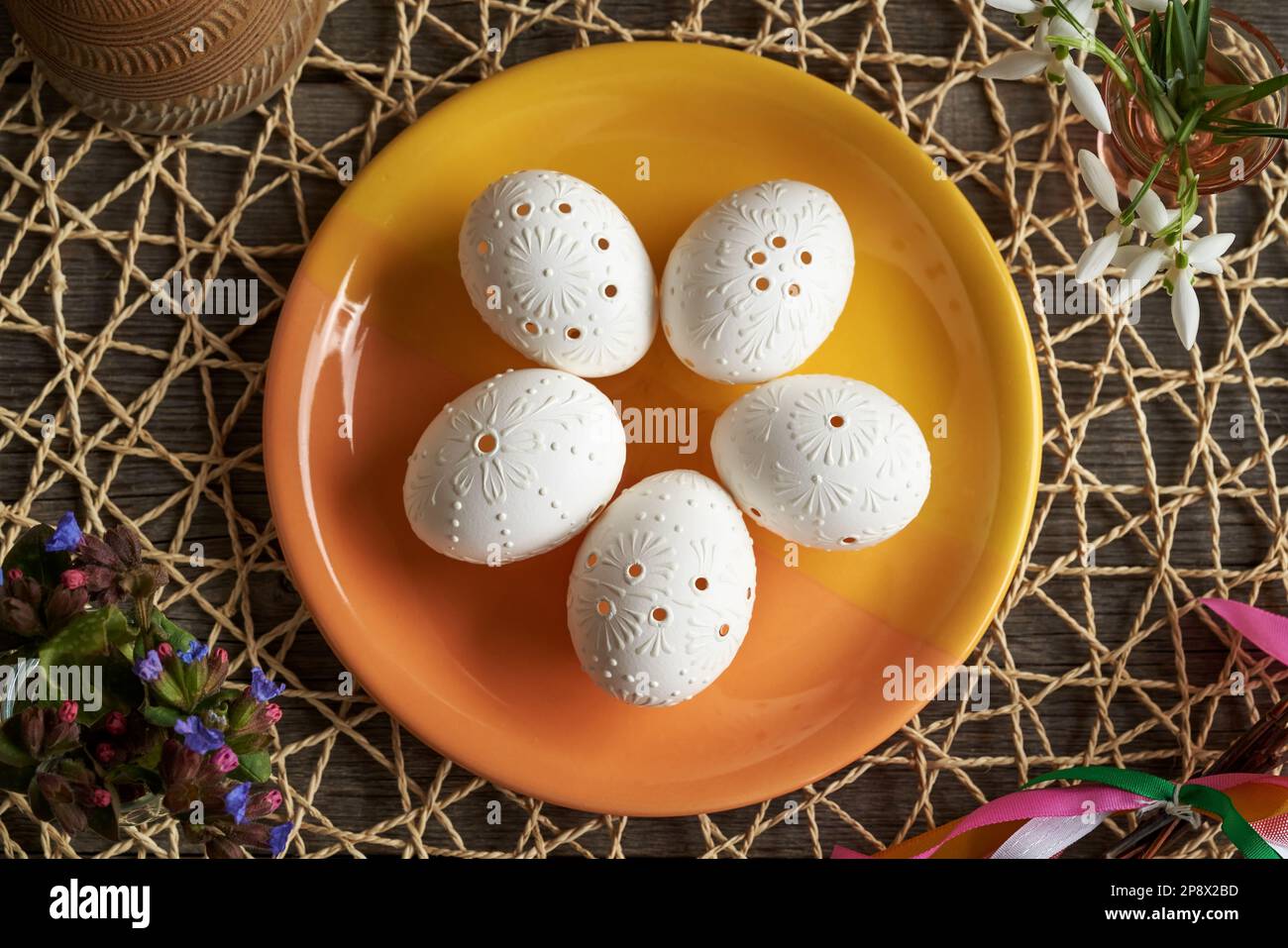 White Easter egg with wax ornaments on an orange plate with spring flowers - snowdrops and ...