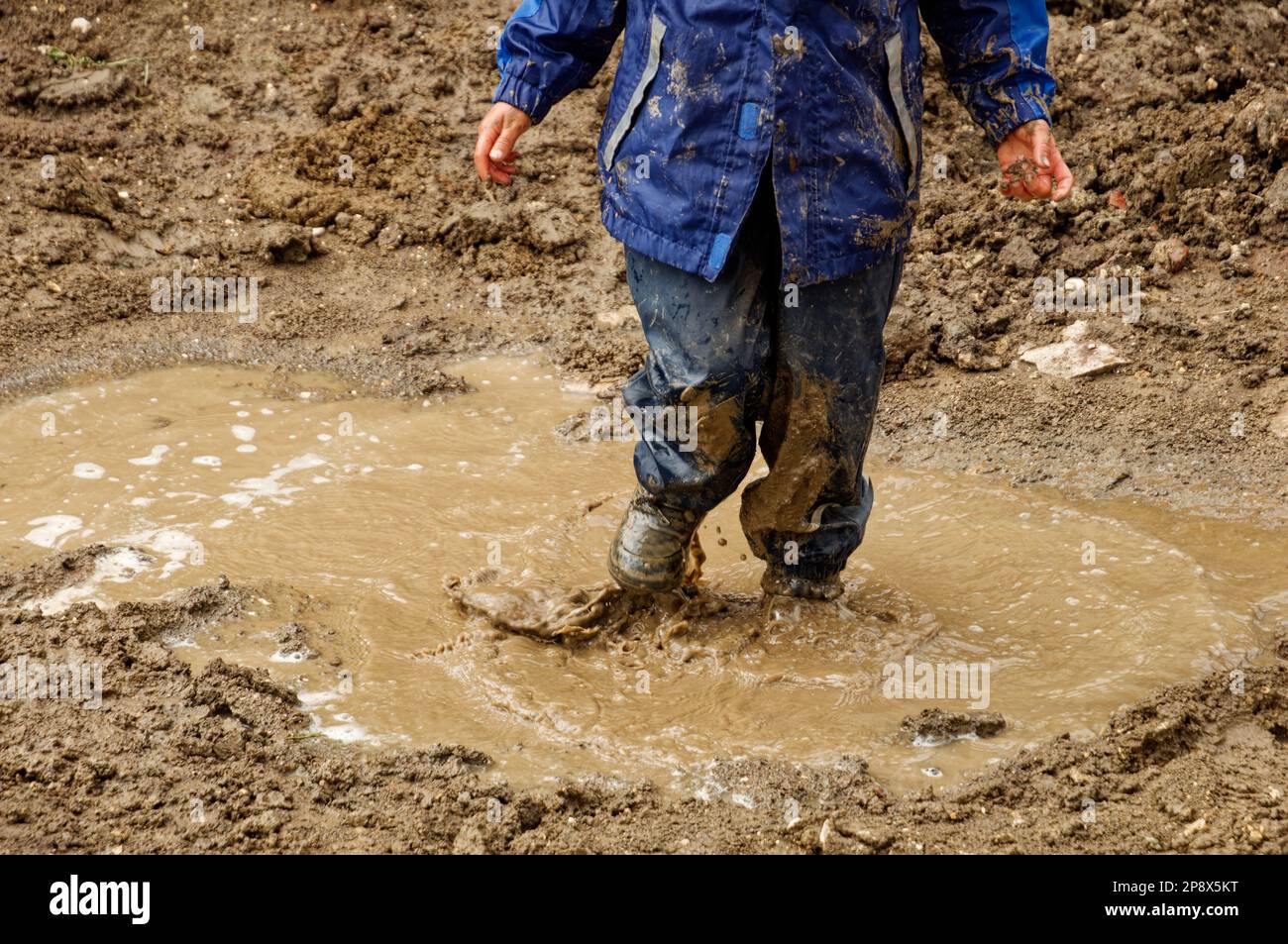 A boy joyfully standing in mud on rainy day, enjoying nature, Germany ...