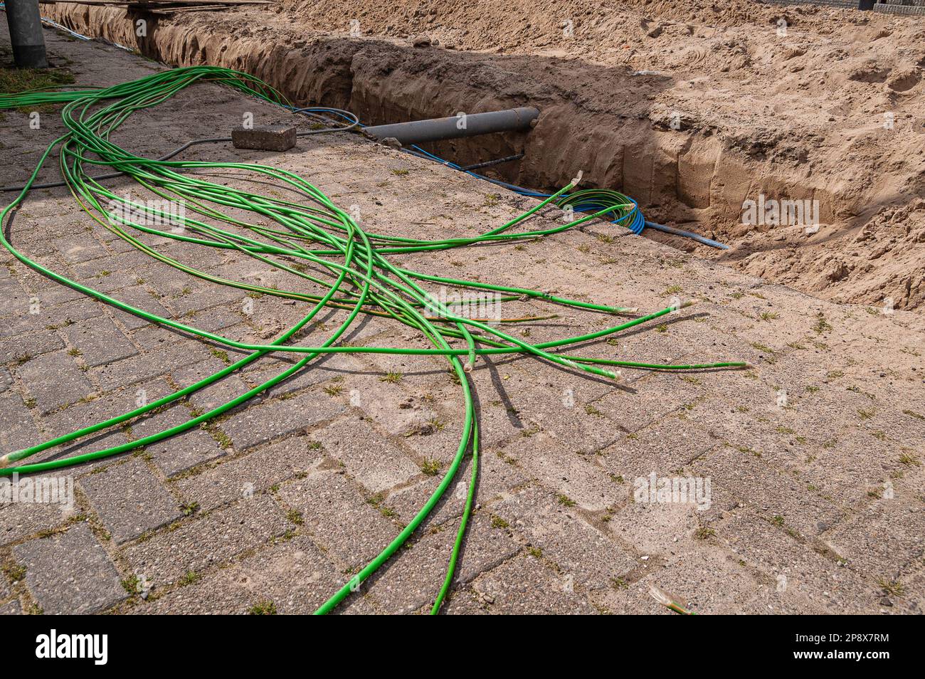 dug sand trench from which green and blue cables lie on the street ...