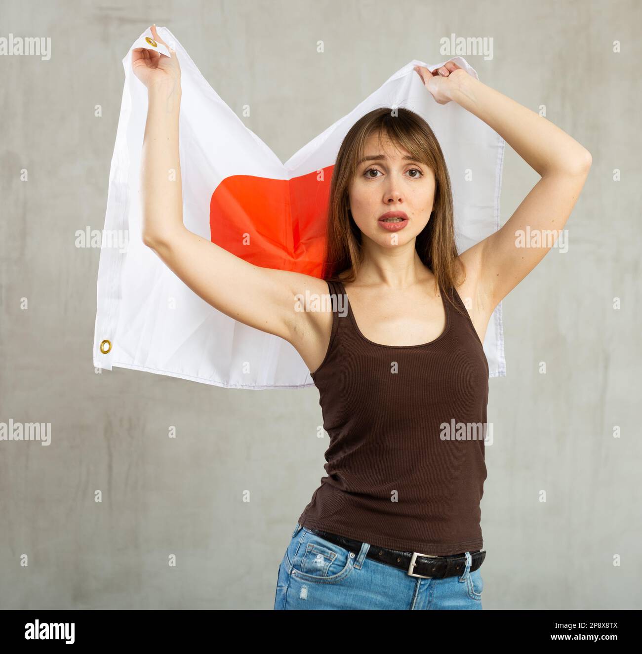 Sad young woman holding flag of Japan against unicoloured background ...